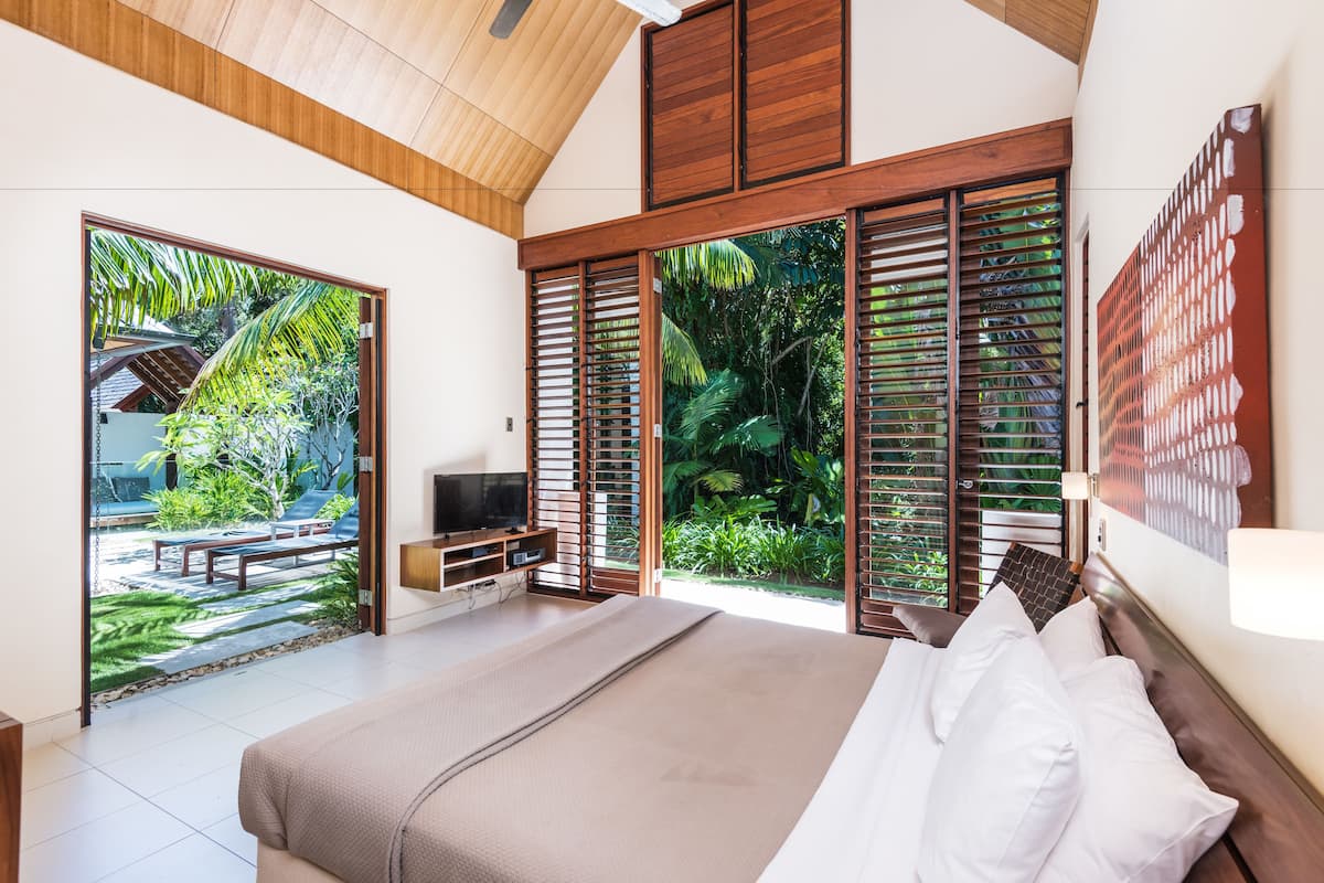 Quarto com uma cama grande, televisão e porta de correr para um jardim.