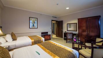 Quarto de hotel com duas camas, uma escrivaninha, uma cadeira, um guarda-roupa e um espelho.
