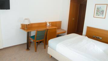 Quarto de hotel com cama, escrivaninha, cadeira, luminária e quadro na parede.
