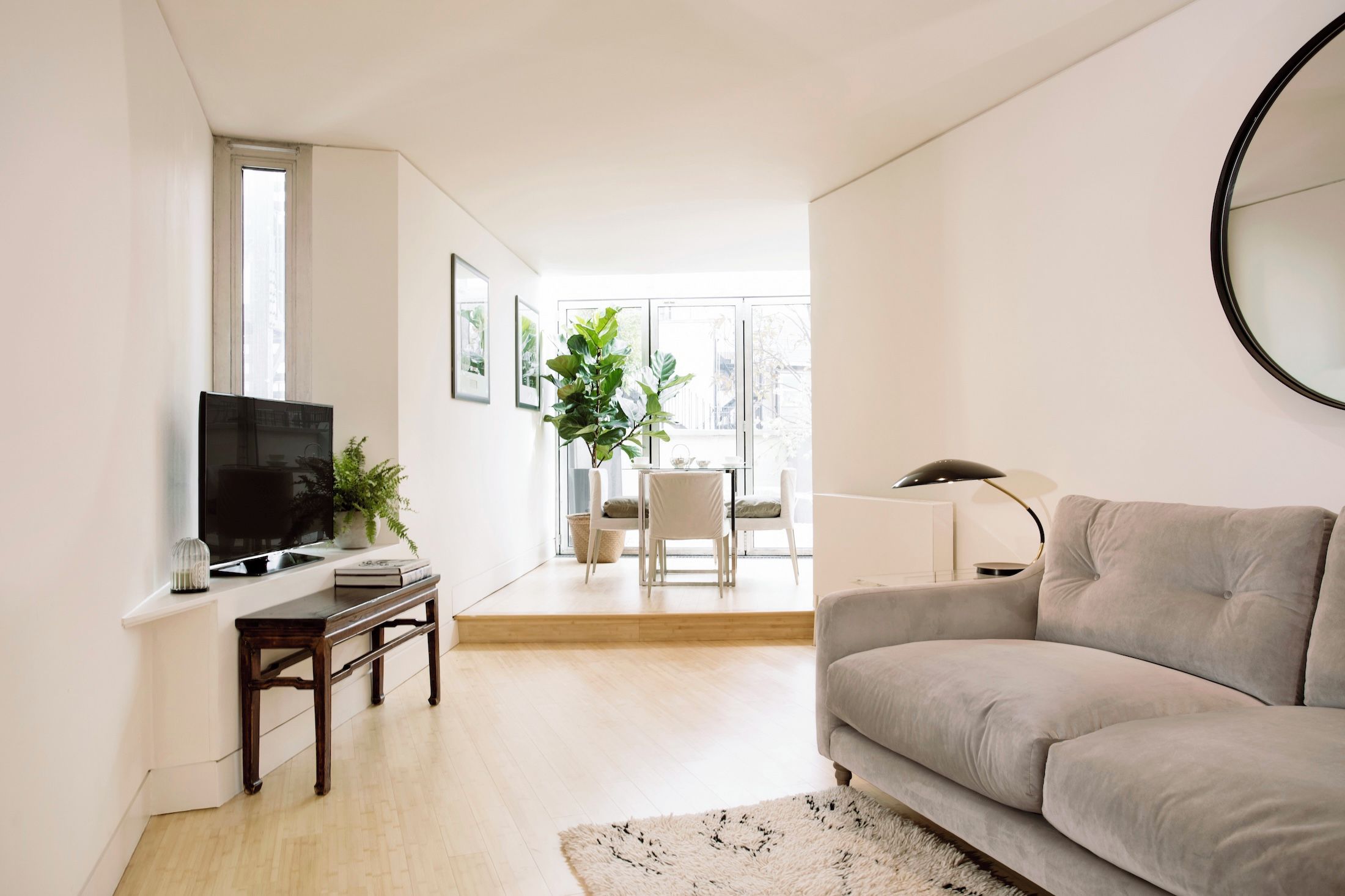 Uma sala de estar moderna com sofá, televisão, área de jantar com cadeiras e uma janela grande.