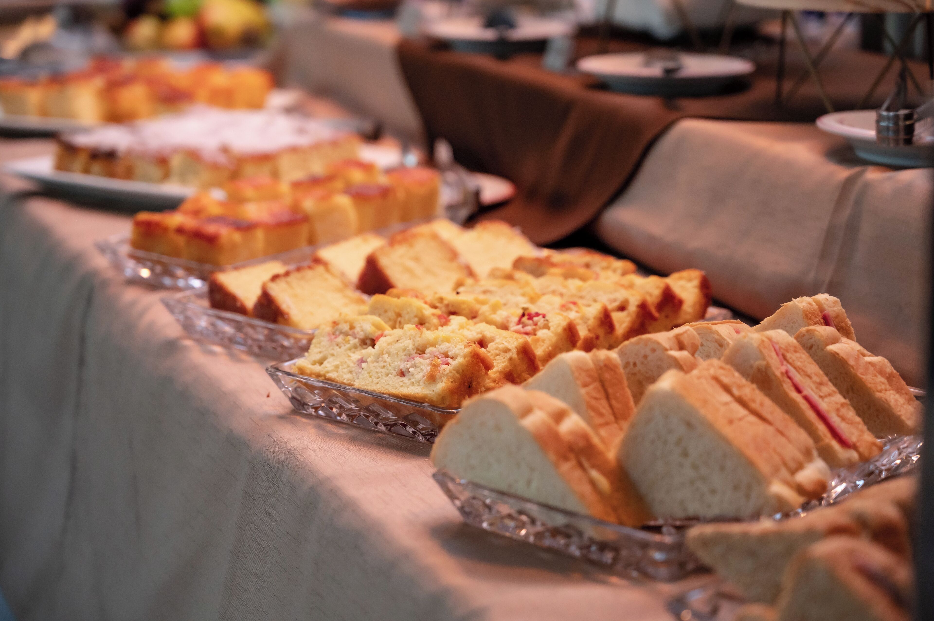 Uma mesa de buffet com diversos tipos de sanduíches e sobremesas.