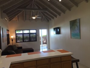 Uma cozinha ampla com uma ilha grande, um ventilador de teto e uma TV fixada na parede.