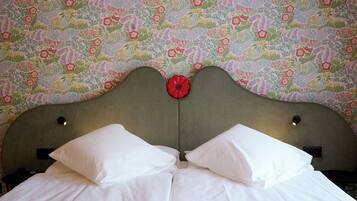 Uma cama com roupa de cama branca, cabeceira decorada com detalhes vermelhos e papel de parede estampado com flores.