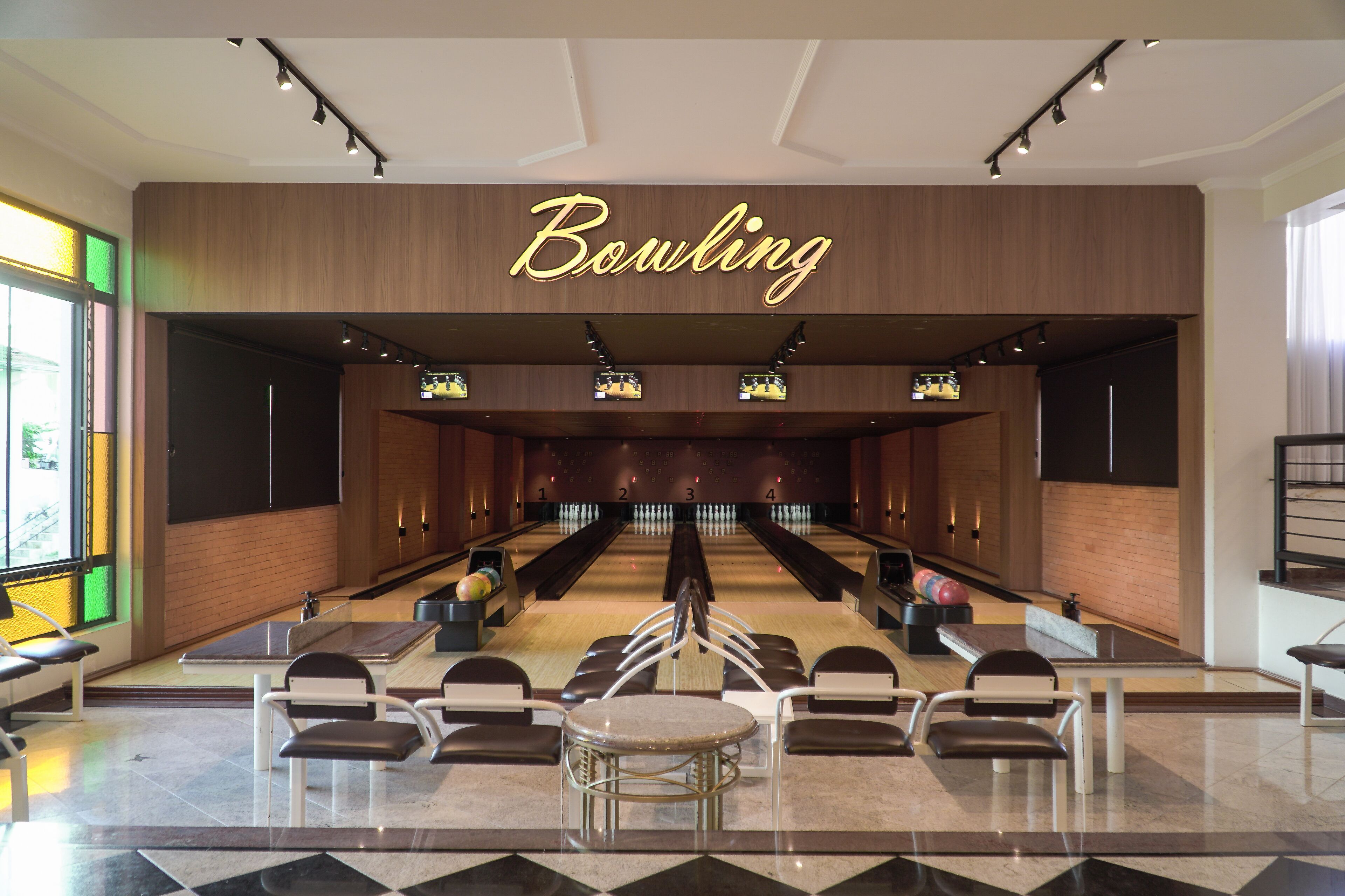 Uma pista de boliche com várias pistas, áreas de estar e um letreiro de neon com a palavra "Bowling".