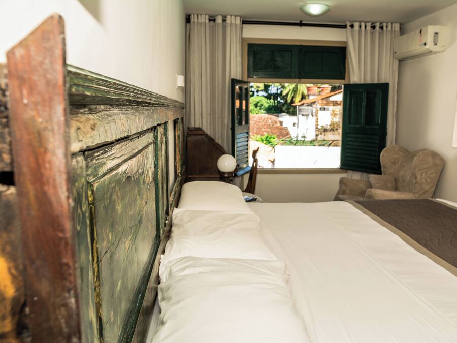 Quarto com cama, uma cadeira, janela com cortinas e ar condicionado.