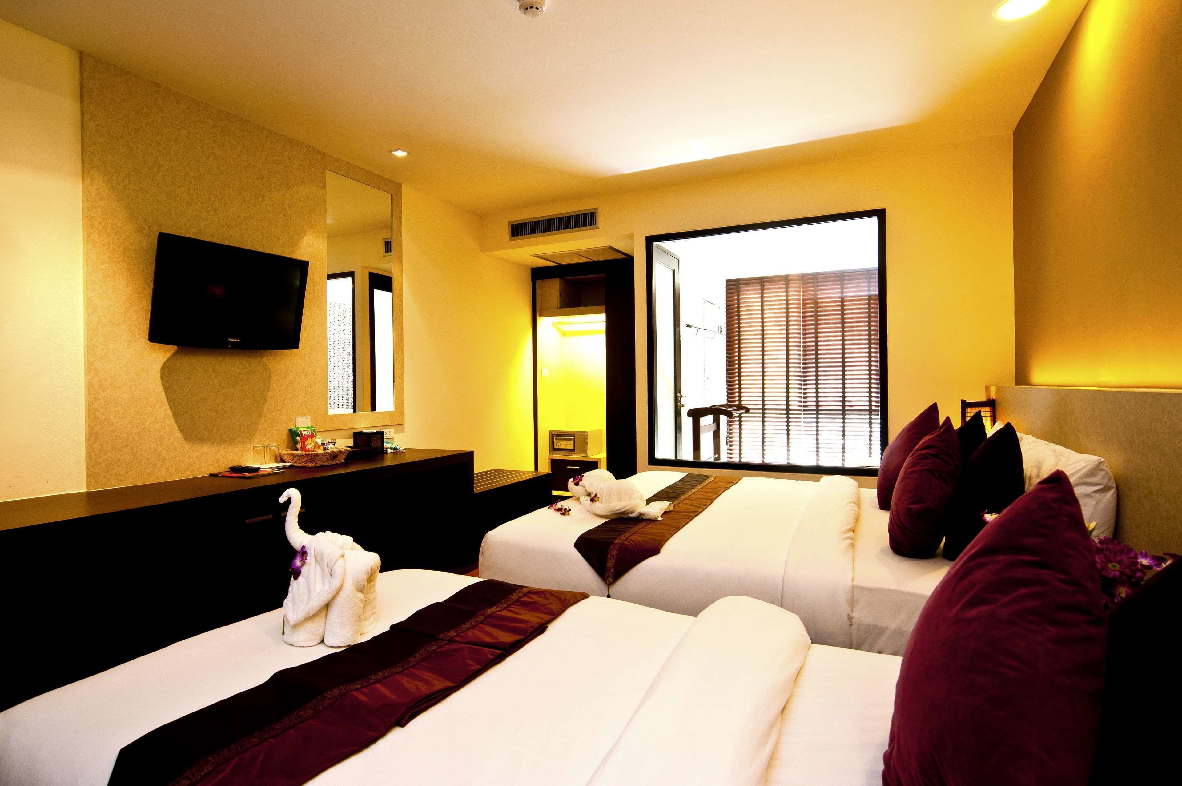 Quarto de hotel com duas camas, televisão fixada na parede, secretária com cadeira e janela com persianas.