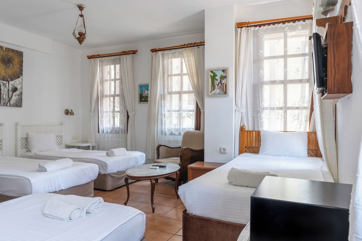 Quarto de hotel com três camas, uma mesa pequena, uma cadeira e uma televisão.