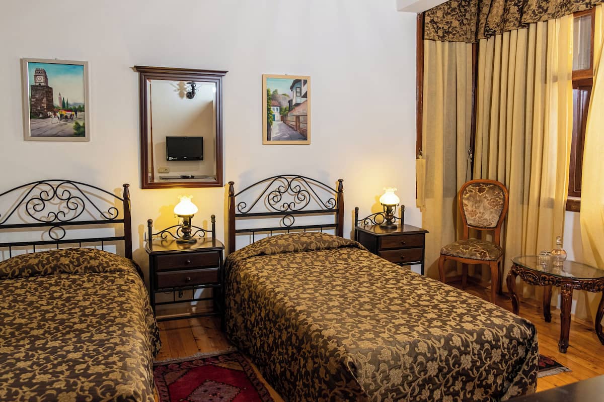 Quarto de hotel com duas camas, um espelho, uma cadeira e uma mesinha.
