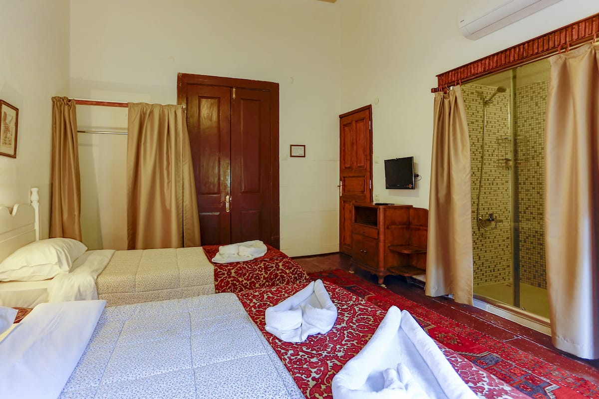 Quarto de hotel com duas camas, um guarda-roupa, uma secretária e área de chuveiro.