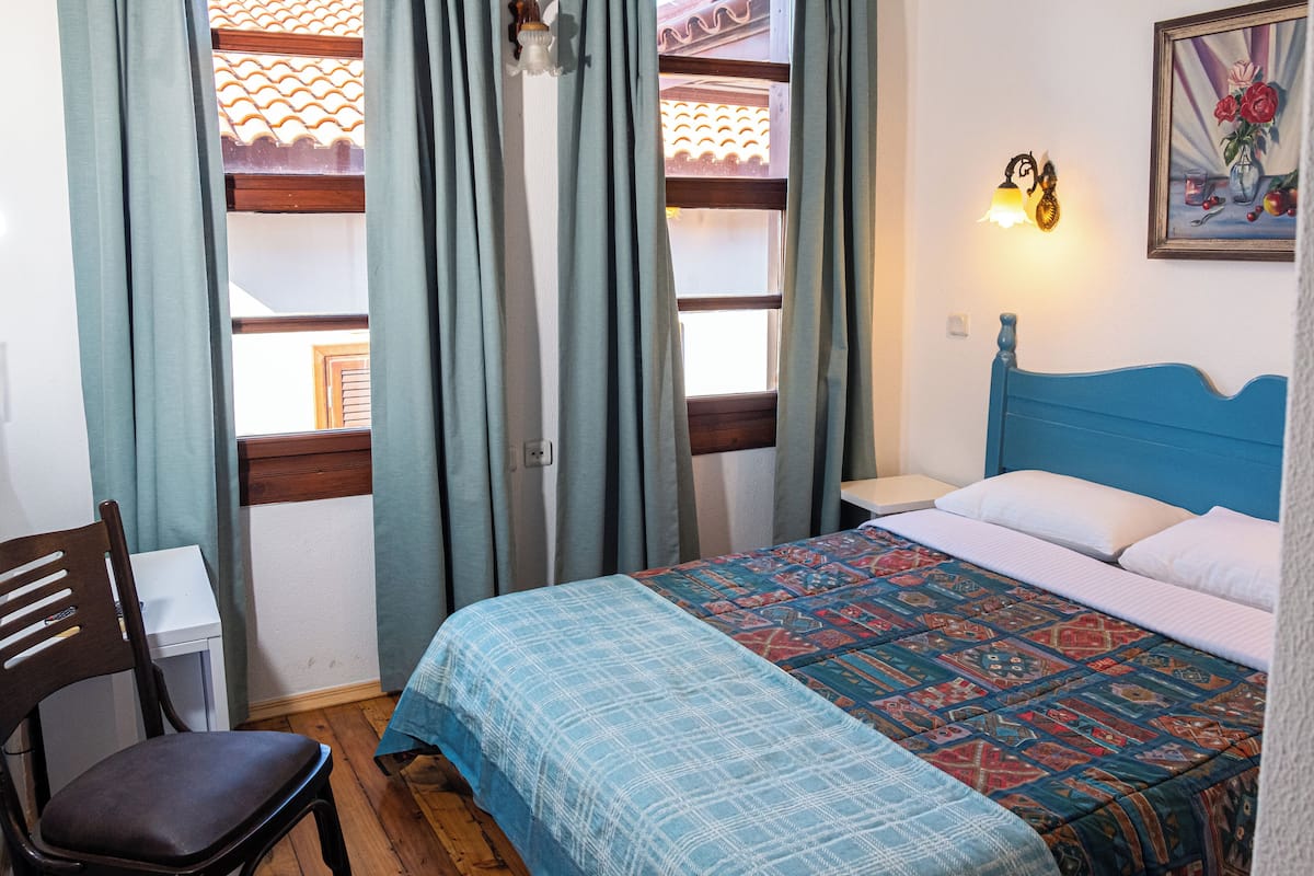Quarto com cama, cadeira, mesa e janela com cortinas.