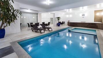 Uma área interna de piscina moderna, com espreguiçadeiras, um balcão de recepção e uma grande planta em vaso.
