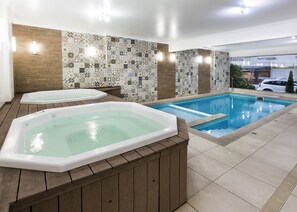 Uma piscina com duas banheiras de hidromassagem, paredes revestidas de azulejo e um deck de madeira.