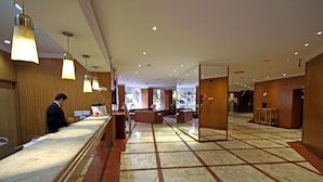 Um hall de hotel com balcão de recepção, área de estar e piso ladrilhado.