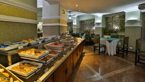 Uma área de buffet com diversos alimentos e um espaço de refeições com mesas e cadeiras.