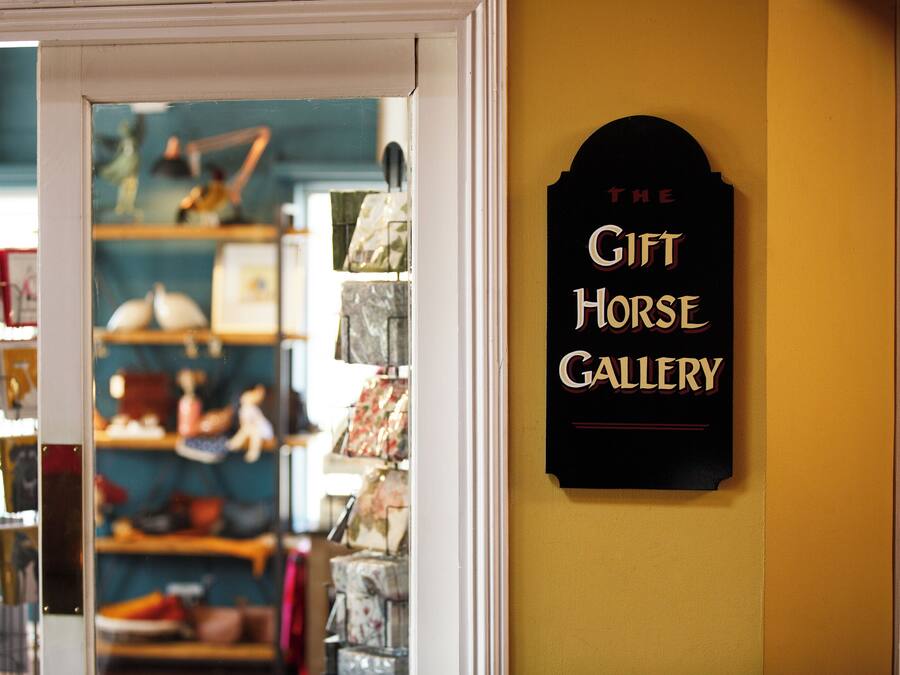 Vitrine com uma placa exibindo "The Gift Horse Gallery" e diversos artigos à mostra no interior.