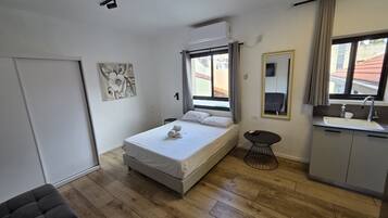 Quarto com cama, mesinha, janela, espelho e guarda-roupa.