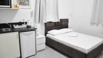 Quarto de hotel compacto com cozinha americana, uma cama e um pequeno frigorífico.