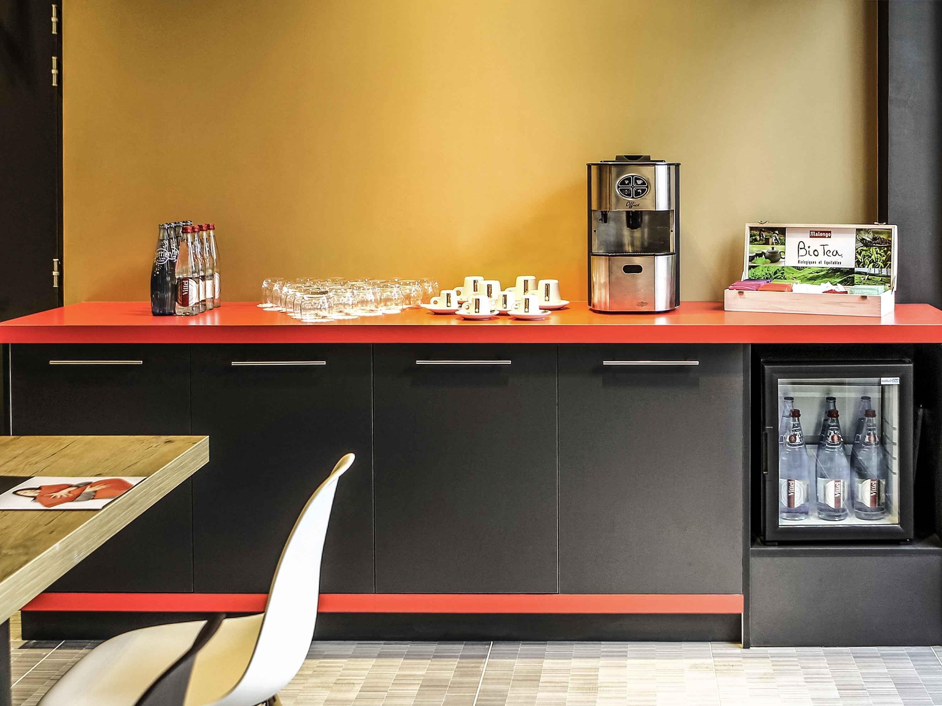 Uma cozinha moderna com cafeteira, geladeira com bebidas e uma seleção de copos e xícaras.