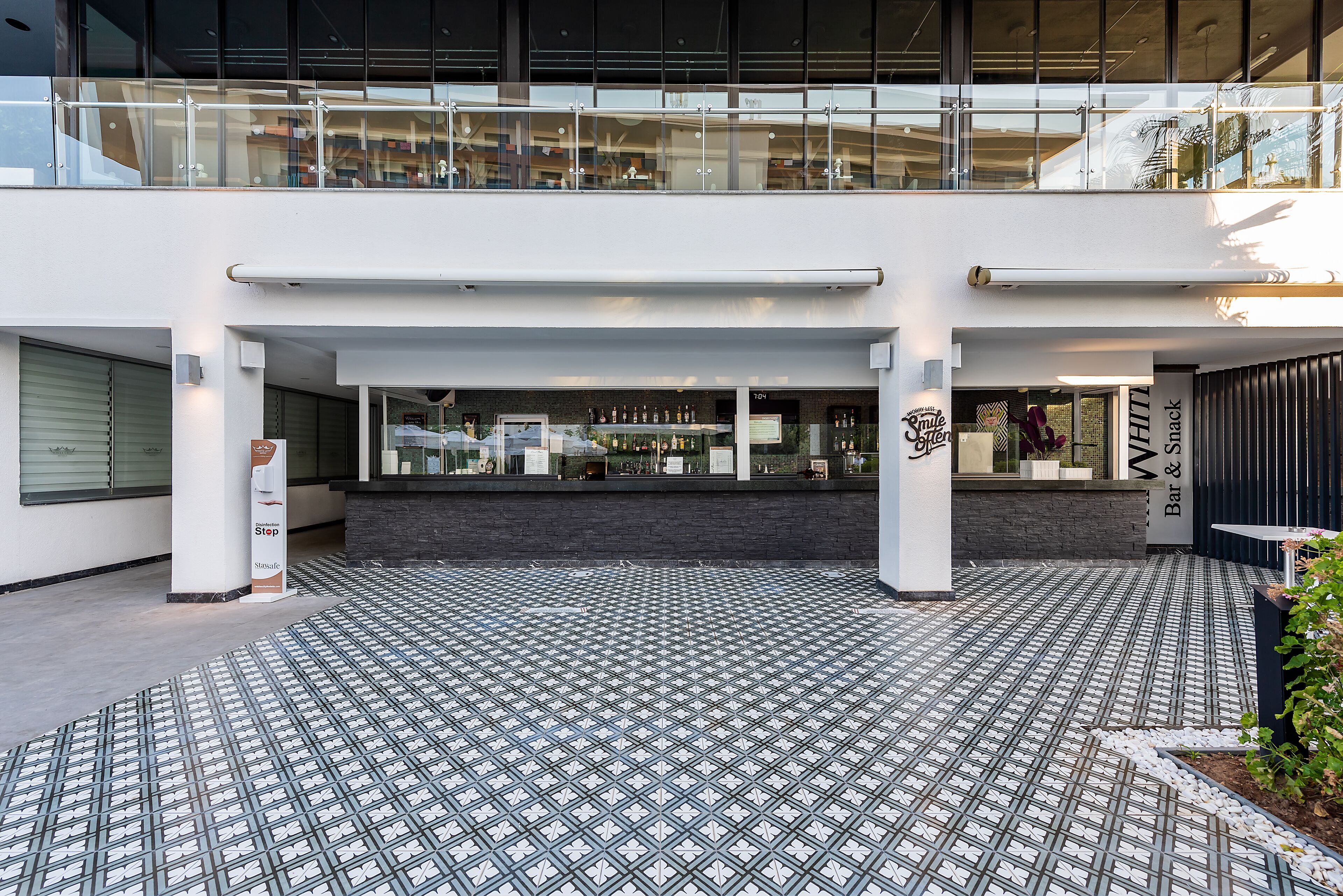 Um edifício moderno com varanda de vidro, piso estampado e sinalização para bar e área de lanches.