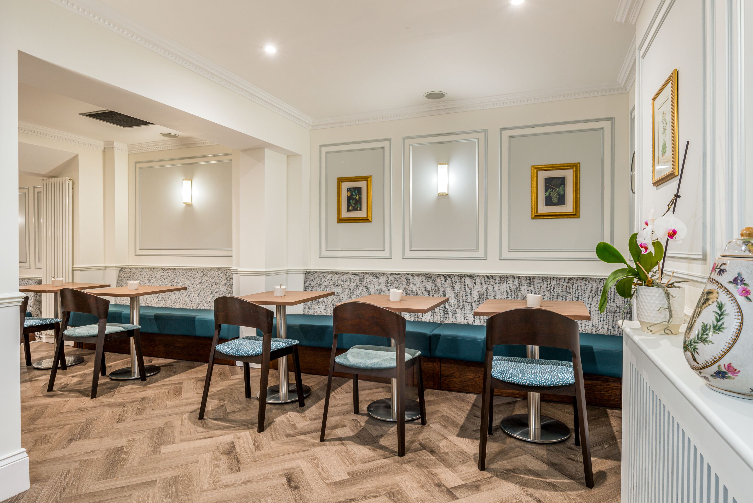 Restaurante com piso de madeira, assentos acolchoados azuis e obras de arte emolduradas nas paredes.