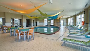 Uma área interna com piscina, cadeiras de descanso e mesas.