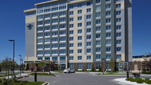 Um hotel com vários andares e design moderno, com uma combinação de fachadas de vidro e pedra, e uma entrada central com galeria coberta.