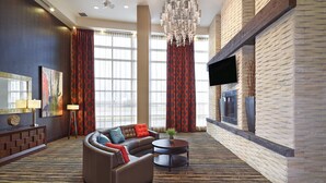 Um lobby de hotel moderno com um sofá de couro, uma mesa de centro redonda, uma televisão grande fixada numa parede de pedra e um candelabro.