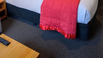 Quarto de hotel com duas camas, cada uma com roupa de cama vermelha e branca, cabeceira de madeira, mesa de cabeceira e um controle remoto no chão.