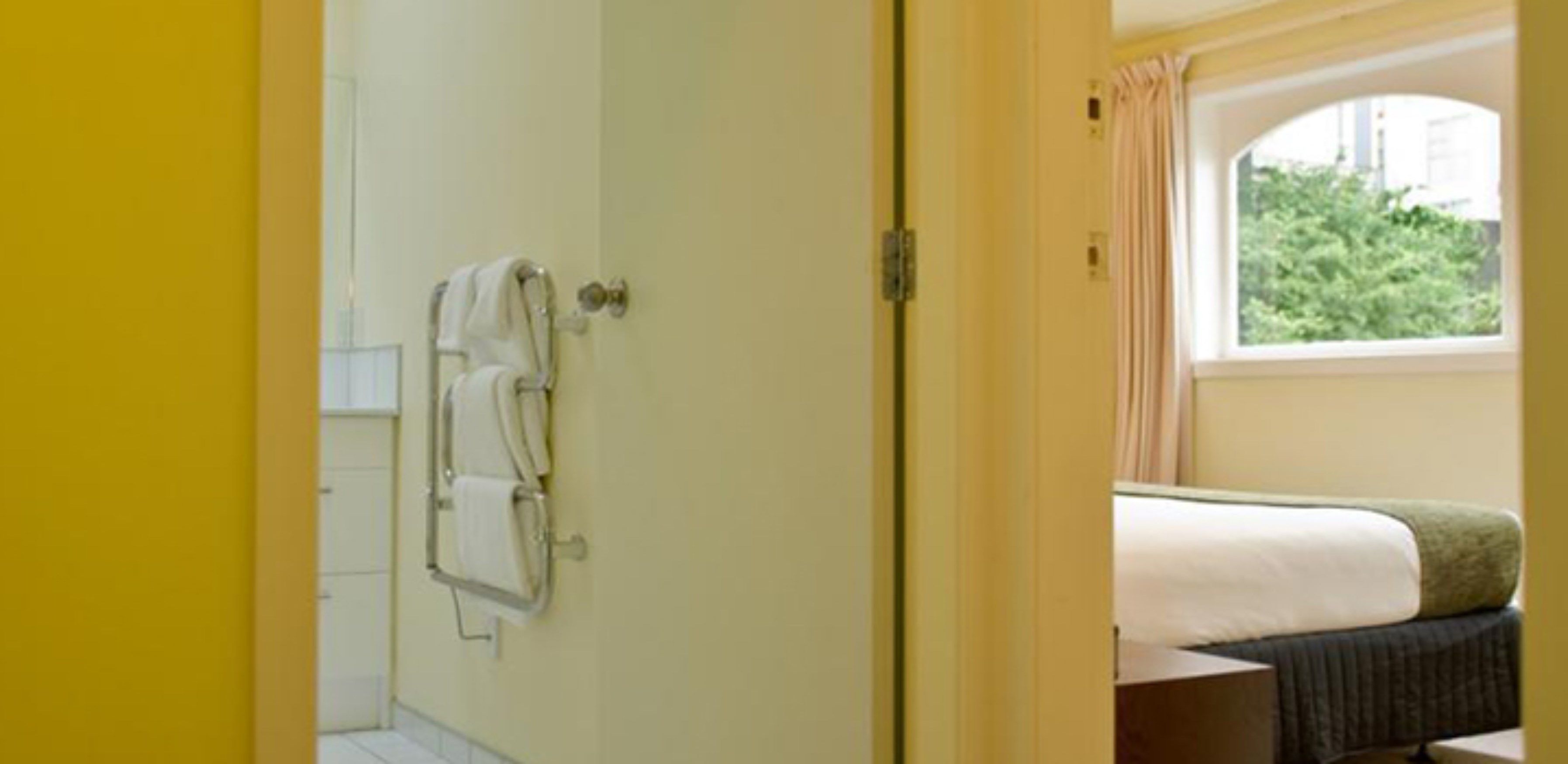Quarto de hotel com uma cama, janela com cortinas e um porta-toalhas com toalhas.