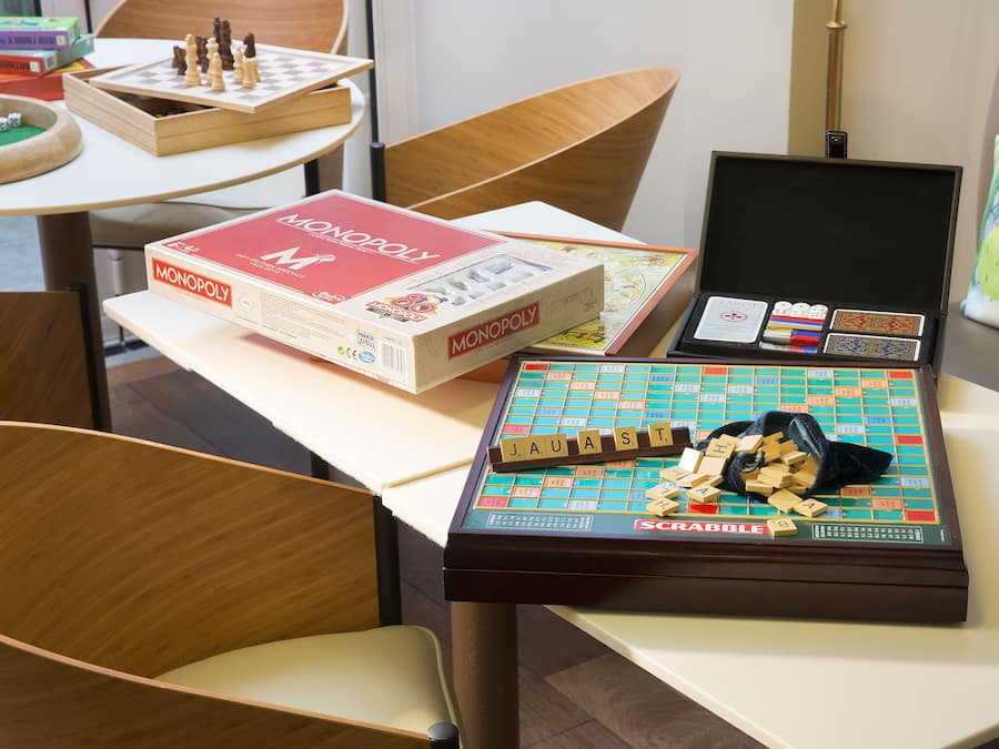 Uma mesa com uma caixa do jogo Banco Imobiliário, peças de Scrabble e um tabuleiro de Scrabble.