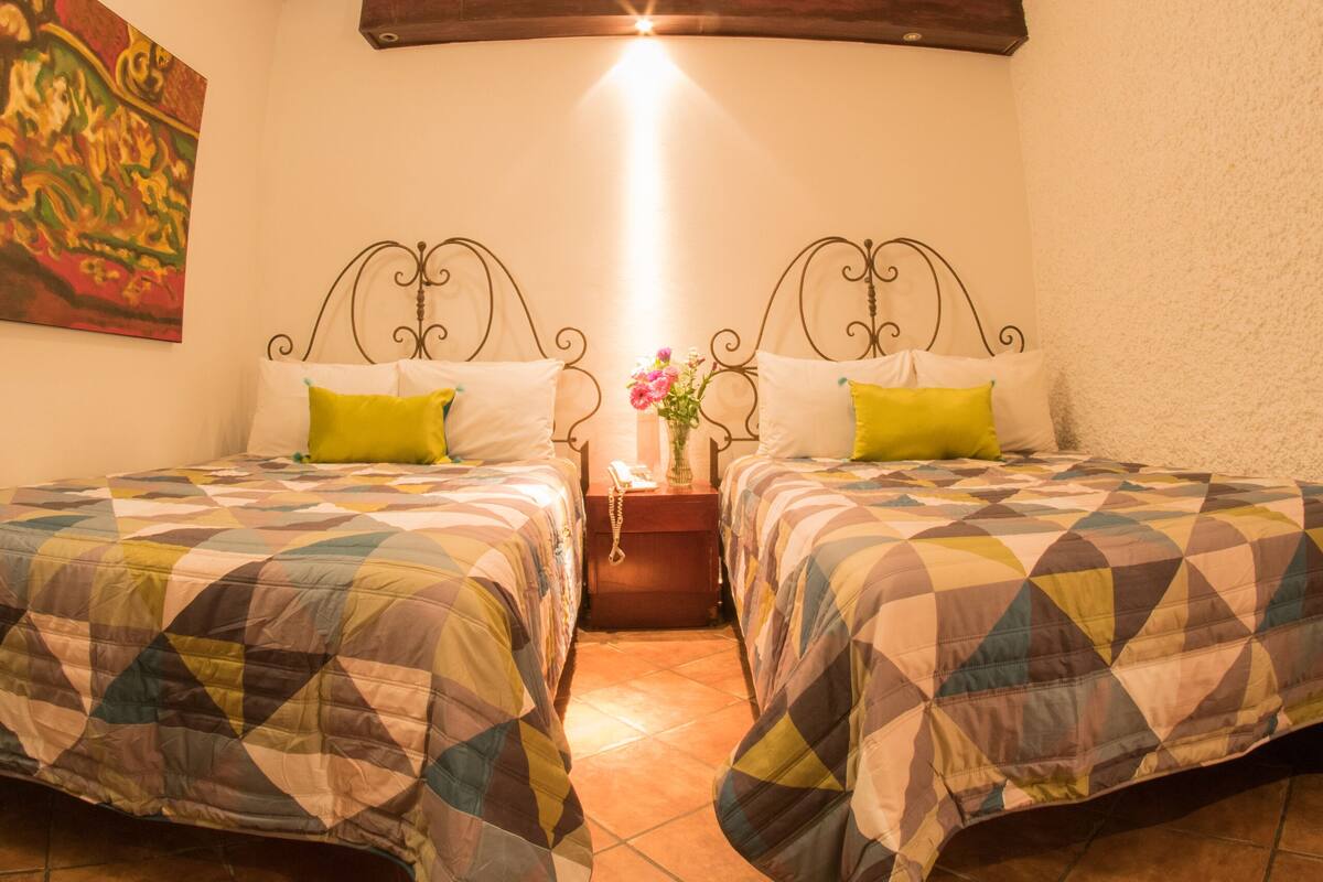 Quarto com duas camas, uma mesa de cabeceira, um quadro na parede e uma luminária no teto.