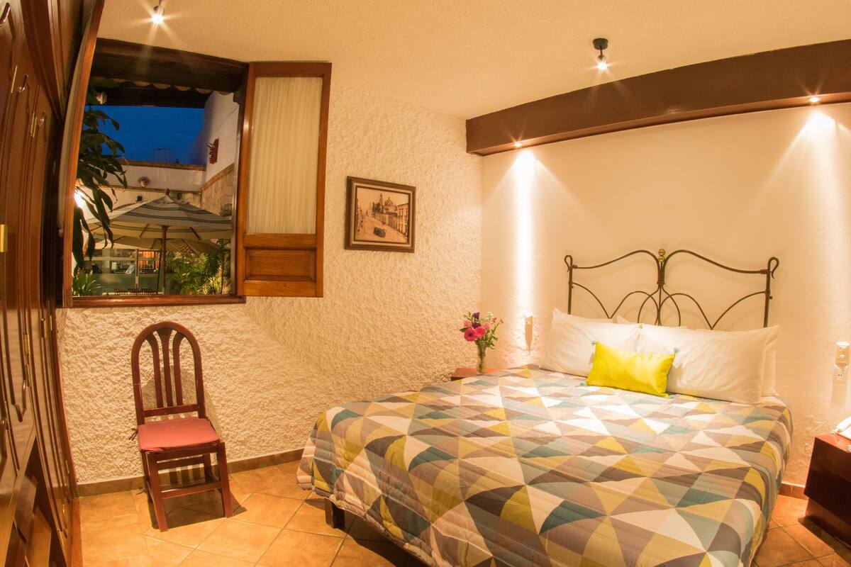 Um quarto com uma cama, uma cadeira, uma janela e uma porta.
