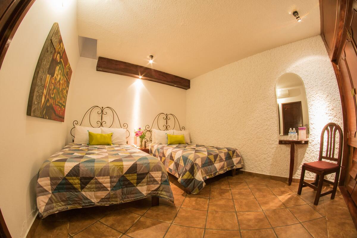 Quarto com duas camas, uma cadeira, uma mesa pequena e um quadro na parede.