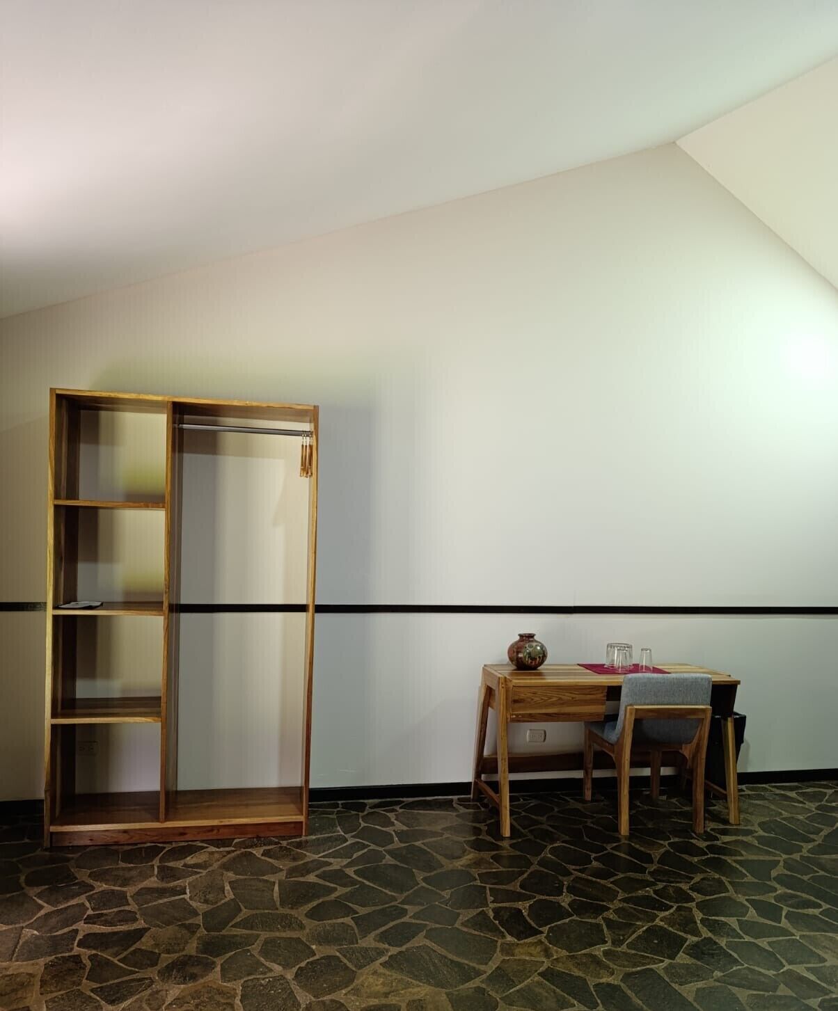 Um quarto com um guarda-roupa de madeira, uma pequena mesa com um vaso e uma cadeira.