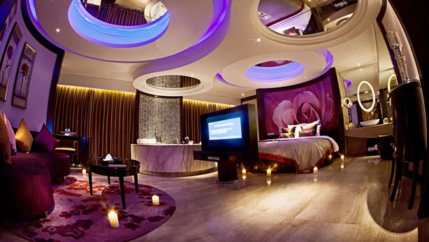 Quarto de hotel luxuoso com design moderno, apresentando uma cama grande, uma televisão, uma toucador com espelho e um domo circular.