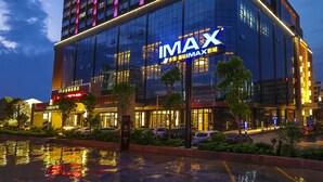 Um hotel moderno com um grande letreiro do IMAX, vários andares e uma superfície aquática refletora na frente.