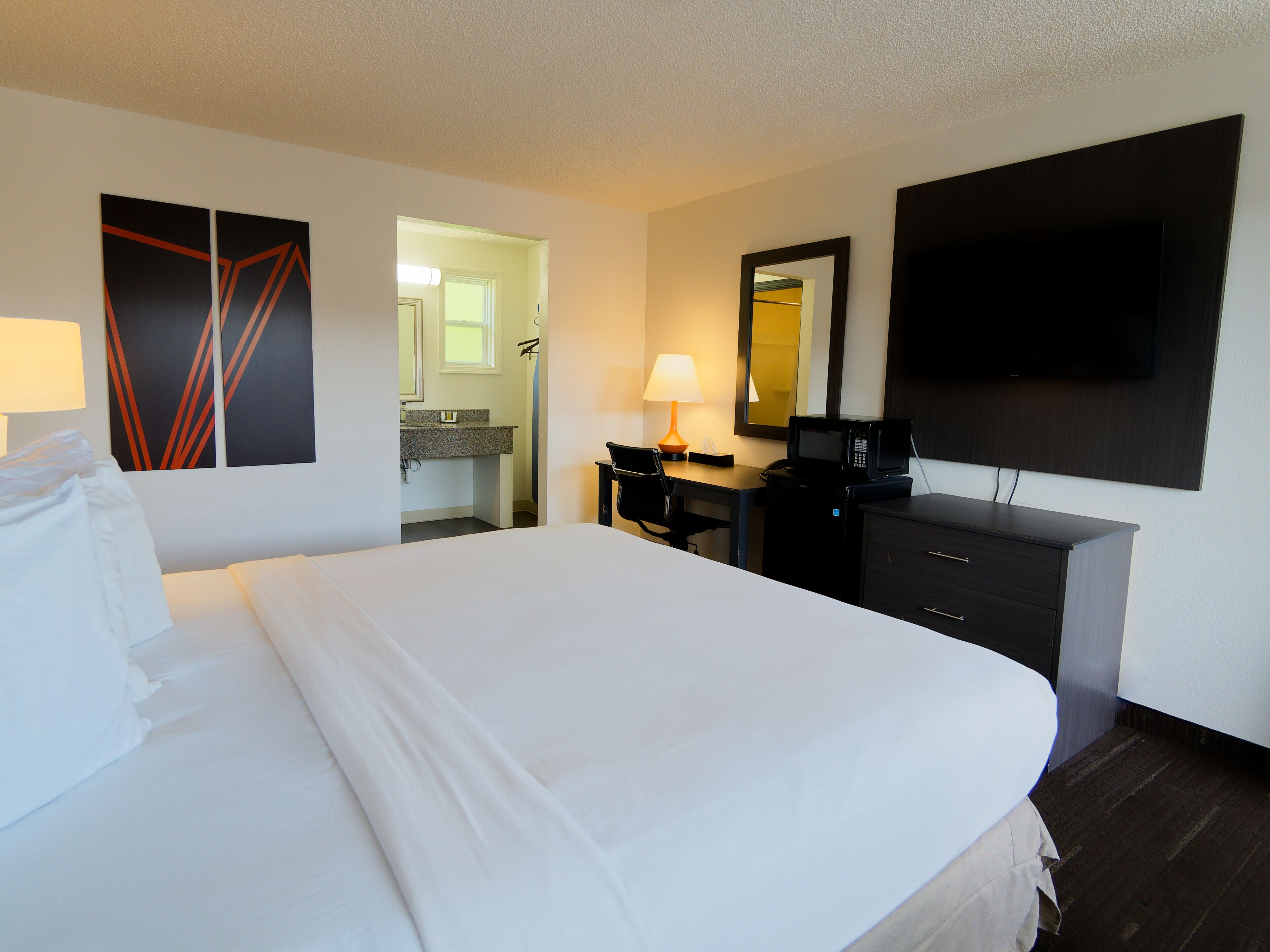 Quarto de hotel com cama, escrivaninha com luminária, televisão e espelho.