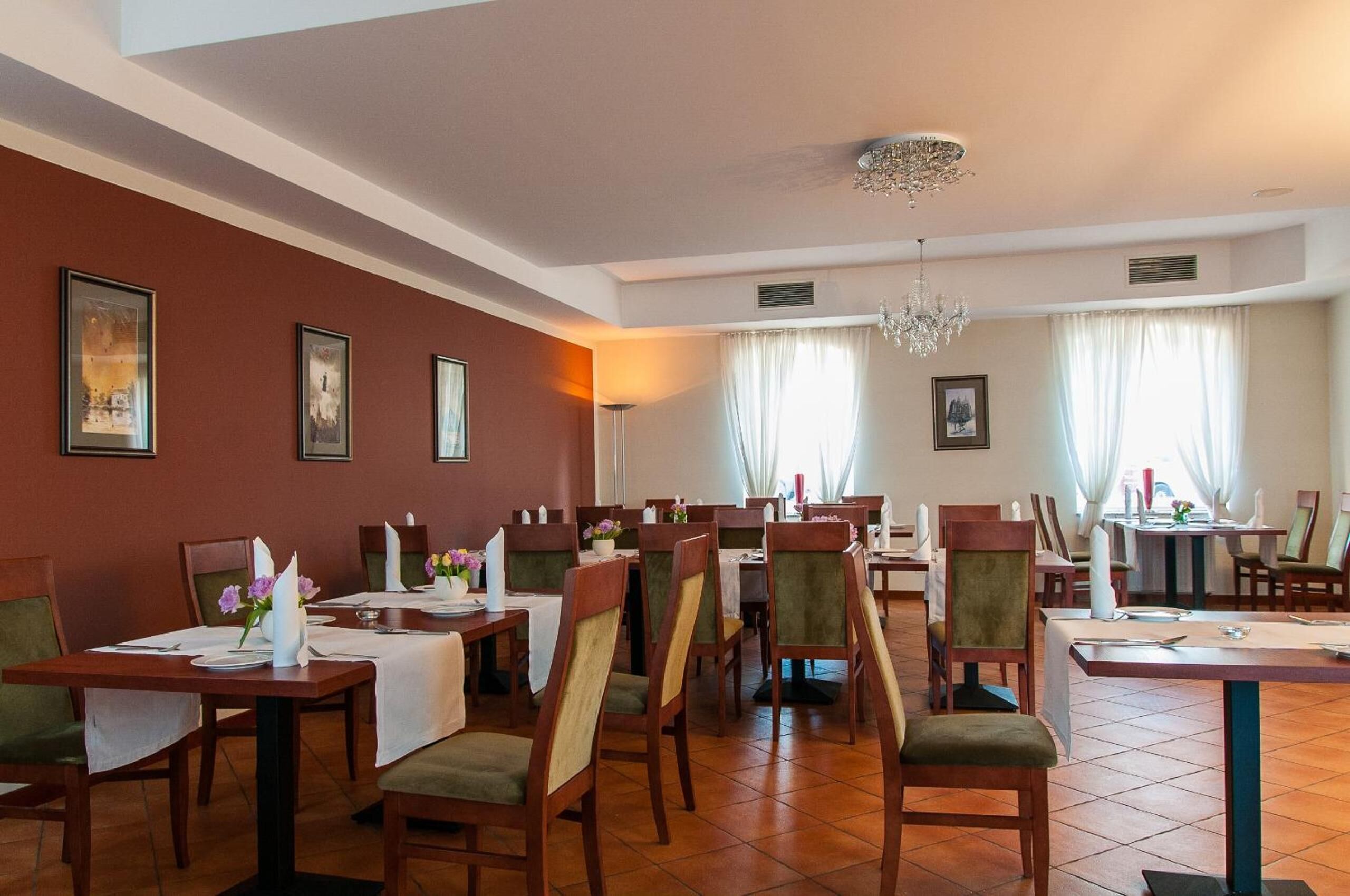 Uma sala de jantar com várias mesas e cadeiras, quadros nas paredes e um candelabro.