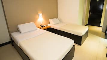 Quarto de hotel com duas camas, uma mesa de cabeceira com abajur e uma porta à direita.