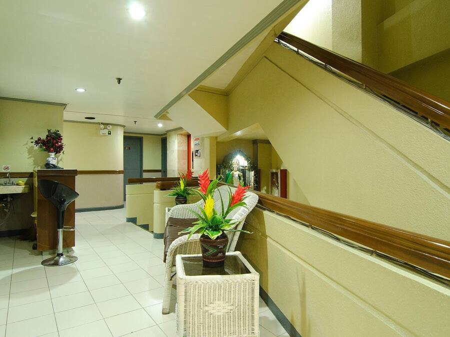 Um saguão de hotel com escadaria, balcão de recepção e área de estar com plantas em vasos.