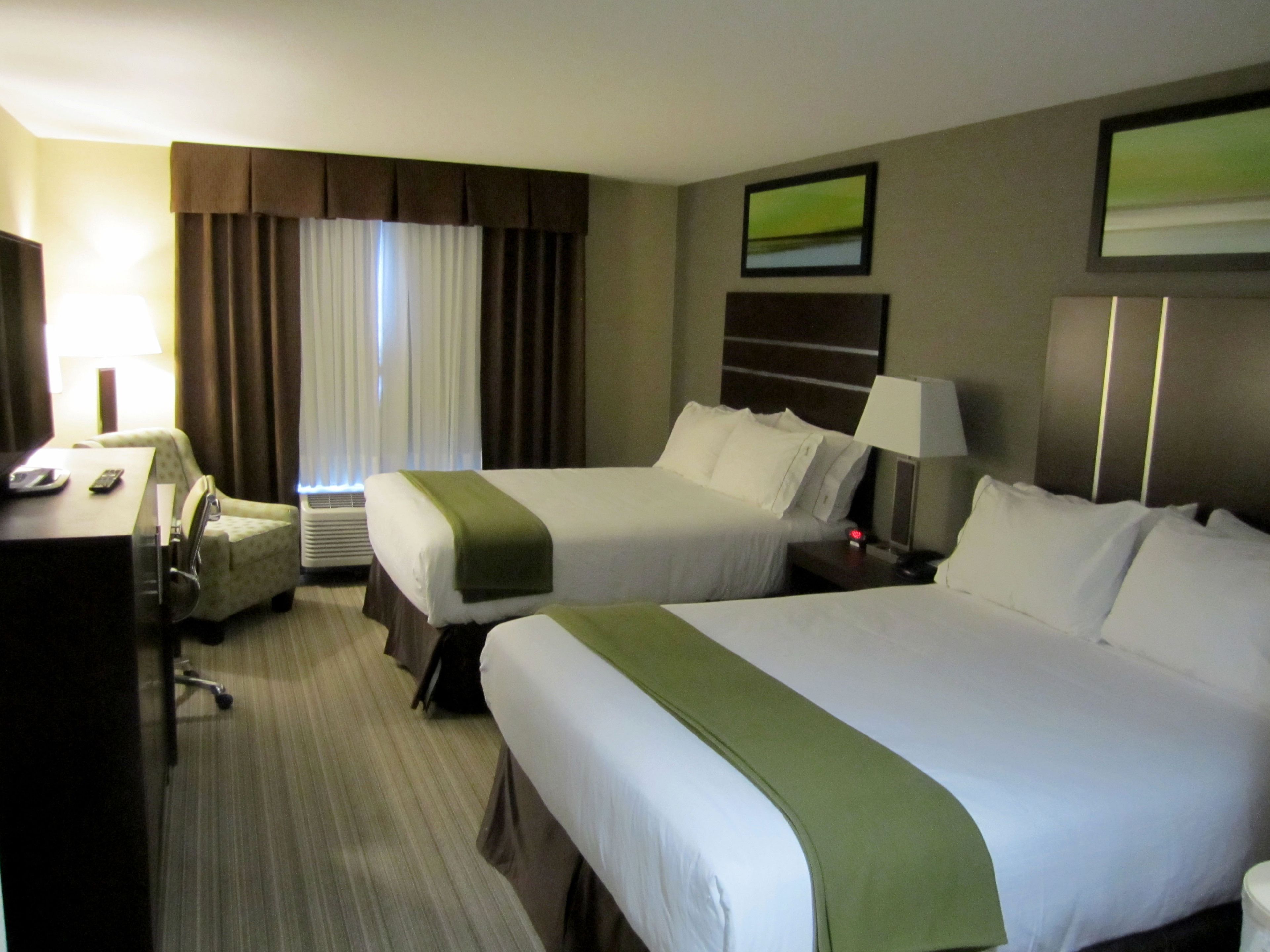 Quarto de hotel com duas camas, uma escrivaninha, uma cadeira, um abajur e uma televisão.