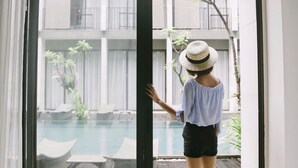 Uma pessoa está em pé em frente a uma porta de vidro deslizante, olhando para uma piscina e um prédio com varandas.