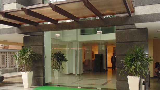 Entrada de hotel com porta de vidro, plantas em vasos e tapete verde.