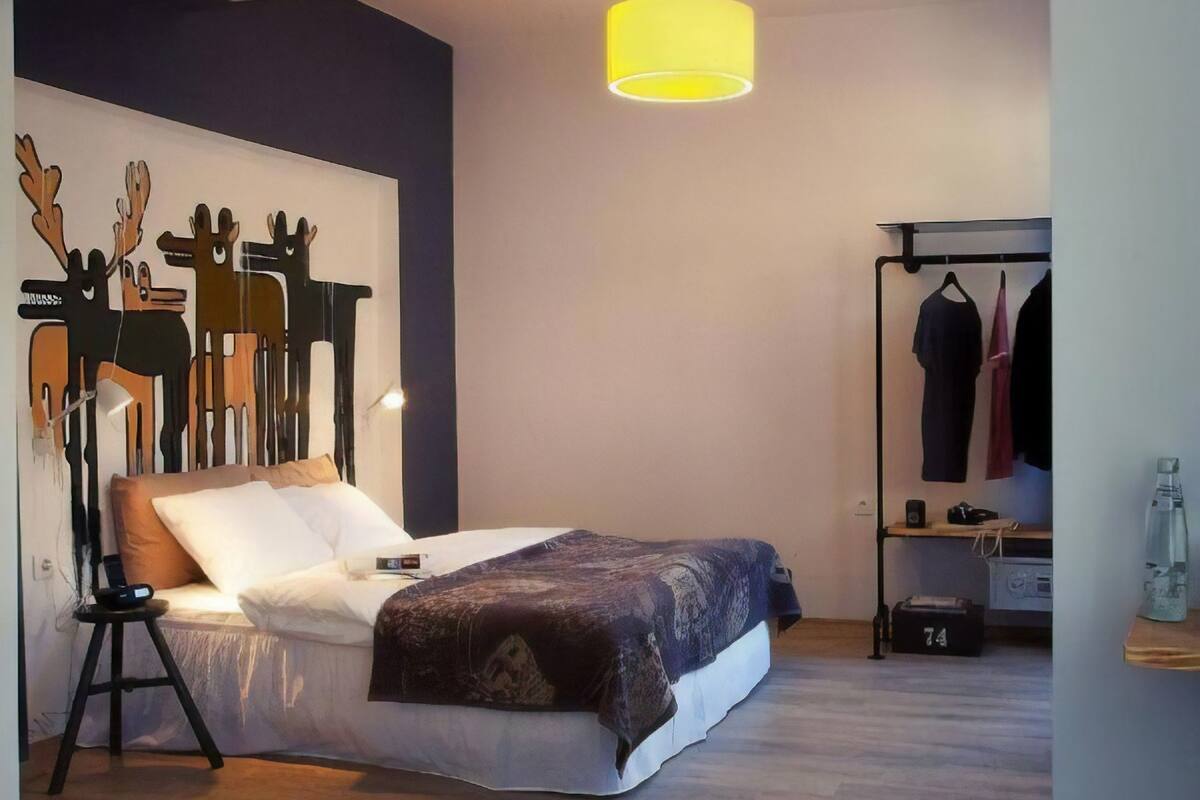 Um quarto moderno com uma cama, um porta-casacos na parede e uma luminária no teto.