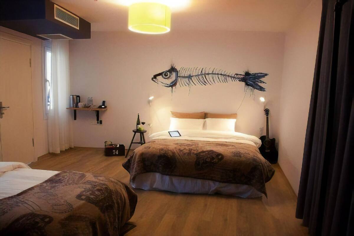 Quarto com cama, uma guitarra, abajur e prateleira com objetos.