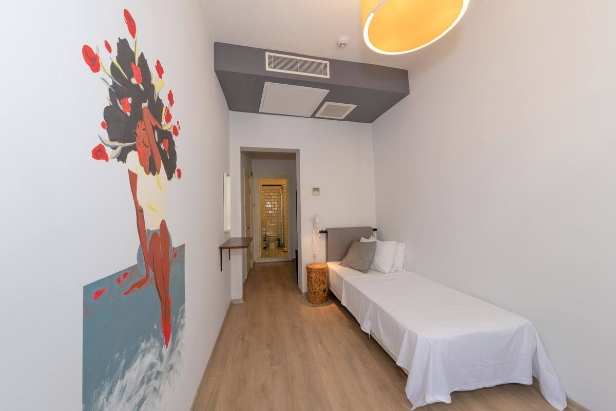 Quarto com cama, mesa de cabeceira, abajur e um quadro na parede.