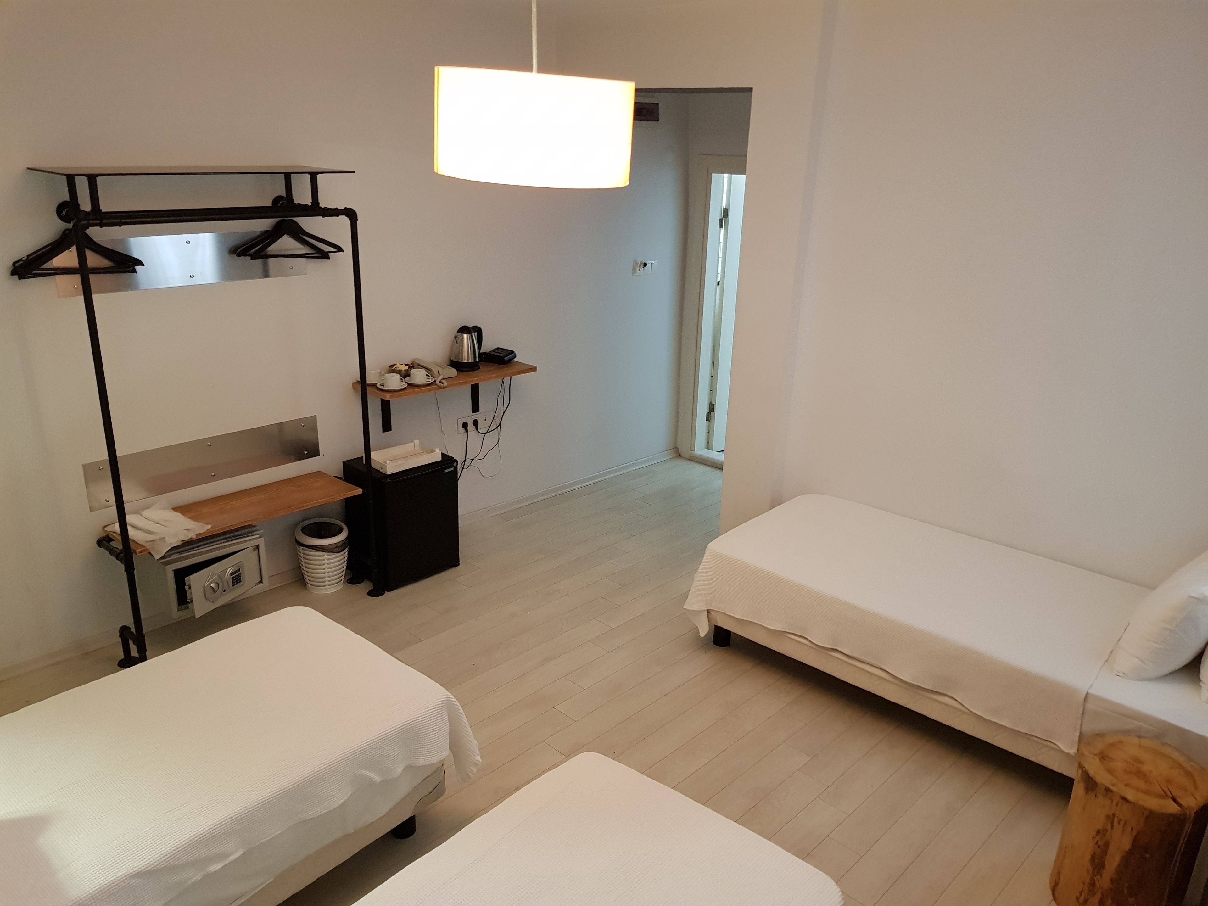 Quarto de hotel moderno com duas camas, uma kitchenette pequena, um cabideiro e vista para o corredor.