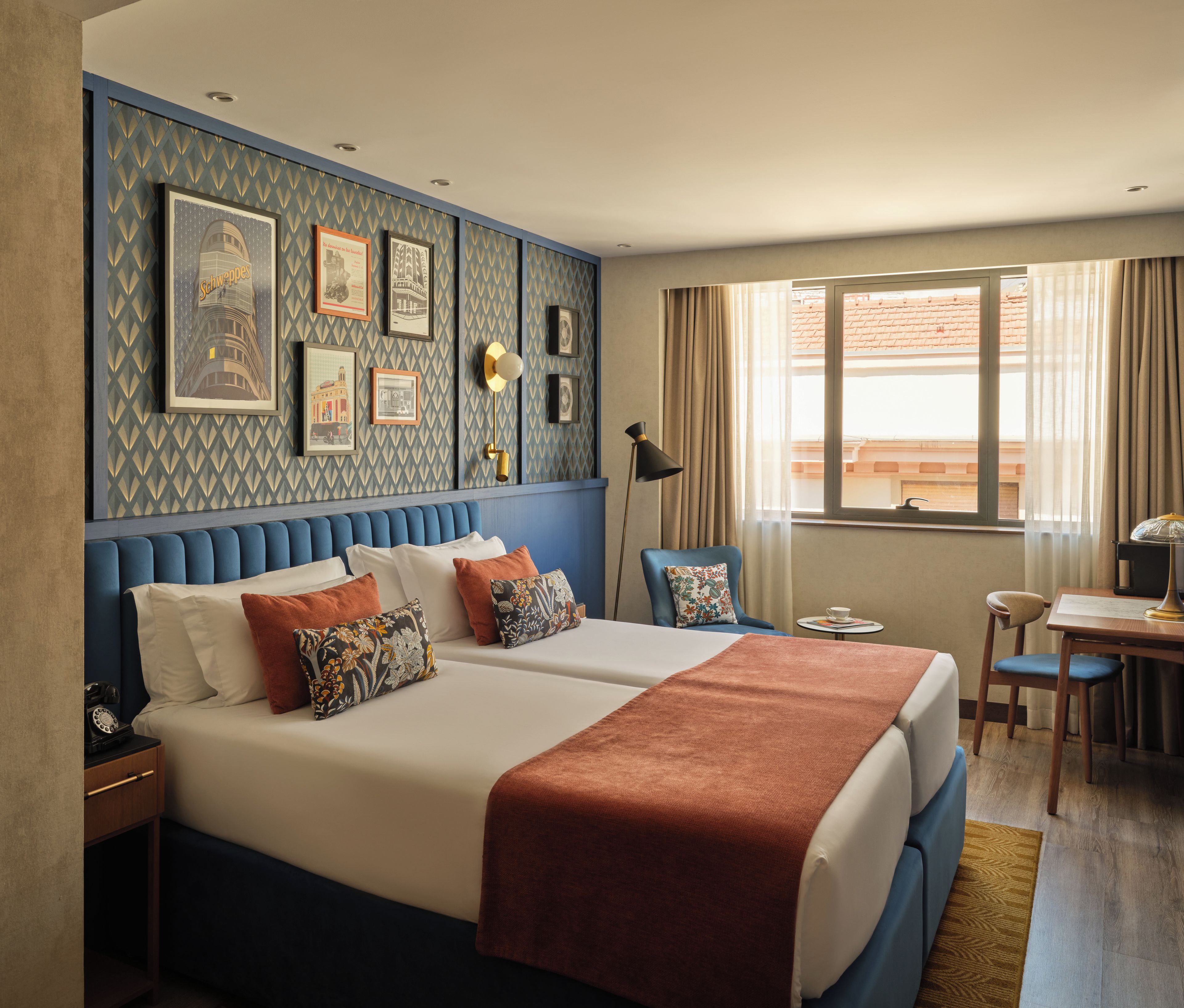 Quarto de hotel com uma cama grande, escrivaninha, cadeira e janela com cortinas.