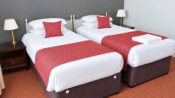 Uma cama de casal com colcha vermelha e branca, duas mesas de cabeceira com abajures e um tapete marrom.