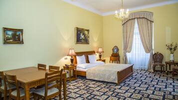 Quarto de hotel com cama, mesas de cabeceira, uma mesa de jantar de madeira com cadeiras, um candelabro e um chão estampado.